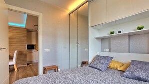 Quarto com cama, mesas de cabeceira, guarda-roupa e um pequeno espaço de estar com uma poltrona e mesa.