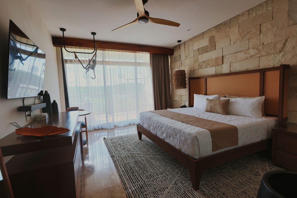 Quarto com cama grande, ventoinha no teto, parede de pedra e vista pela janela.