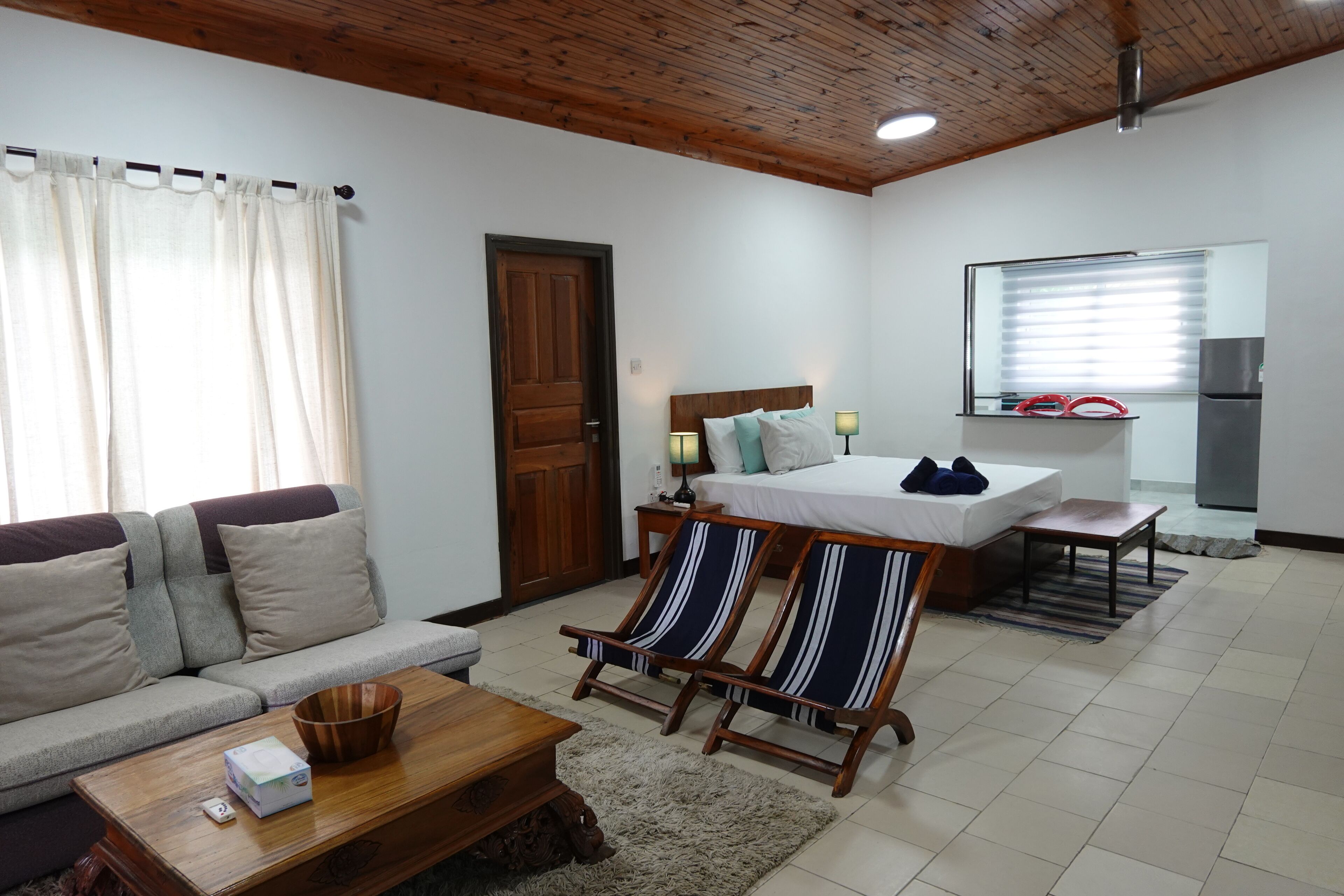 Um quarto com sofá, cama com almofadas, mesa de centro de madeira e uma mesinha com luminária.