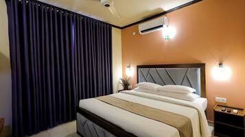 Um quarto com cama, ventilador de teto, ar condicionado, mesa de cabeceira e luminária na parede.