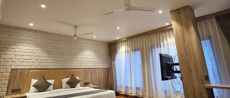 Quarto de hotel moderno com parede de tijolos, uma cama grande, TV de tela plana, ventilador de teto e mesa de centro de madeira.