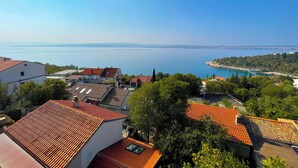 Uma vila costeira com edifícios de telhados em terracota, vista clara do mar e uma ponte ao longe.