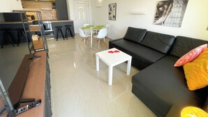 Uma sala de estar moderna com um sofá preto, uma mesa de centro branca e uma área de refeições com uma mesa e cadeiras brancas.