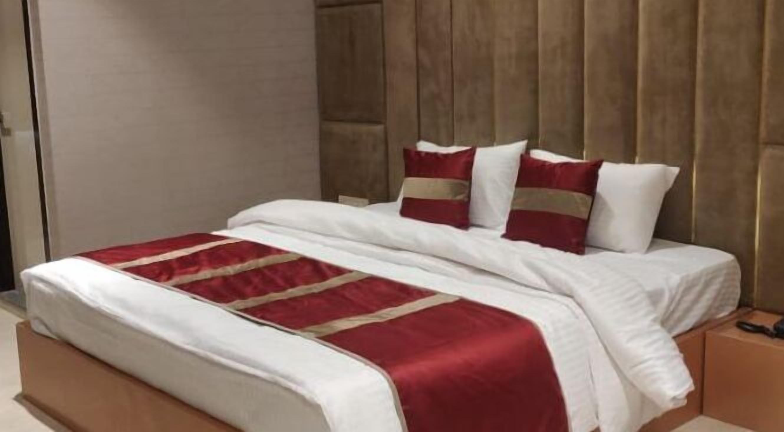 Cama bem arrumada com colcha e almofadas vermelhas e brancas, cabeceira de madeira e mesa de cabeceira de madeira com um telefone.