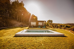 Uma casa moderna com piscina, cercada por um gramado bem cuidado e árvores.