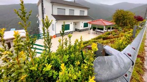 Uma casa de dois andares com telhado de telhas, varanda coberta e vista para as montanhas.