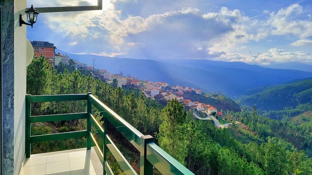 Varanda com guarda-corpo verde com vista para uma vila situada num vale, com montanhas ao longe.