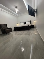 Quarto de hotel moderno com uma cama grande, uma poltrona marrom escura e uma televisão de tela plana fixada na parede.