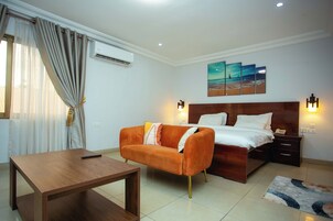 Quarto de hotel com cama, sofá, mesa de madeira e um quadro na parede.
