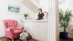 Uma área de recepção com uma cadeira estampada em rosa, uma mesa com uma bolsa e uma planta em vaso.