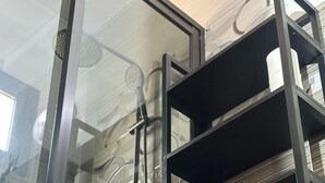 Um banheiro moderno com box de vidro, vaso sanitário branco e estante de metal preta.
