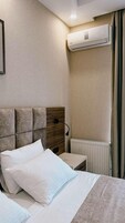 Quarto de hotel com cama, mesa de cabeceira, ar condicionado e janela com cortinas.