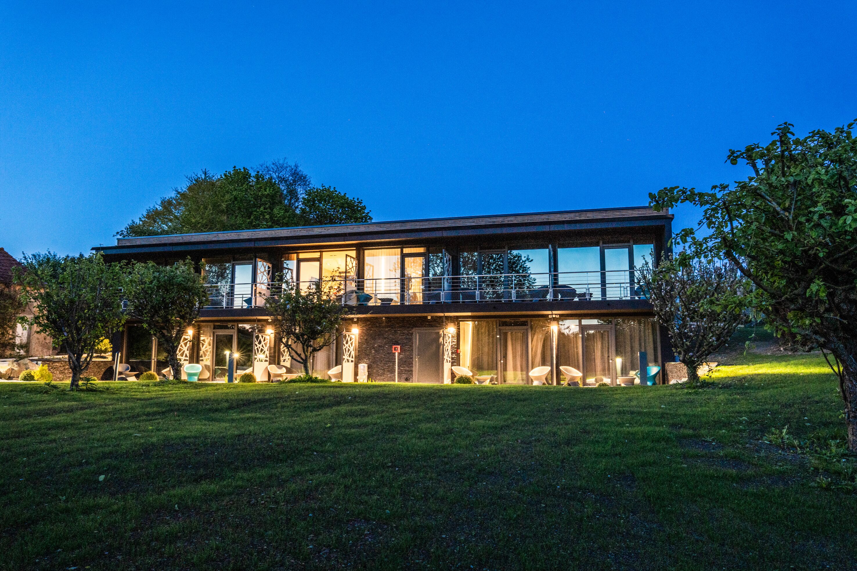 Uma casa moderna de dois andares, com grandes janelas, telhado plano e fachada bem iluminada.