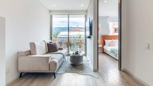Uma sala de estar moderna com sofá, mesa de centro e vista para uma varanda com plantas.