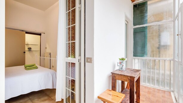 Quarto com cama, uma mesinha com um vaso e porta de vidro deslizante para uma varanda.