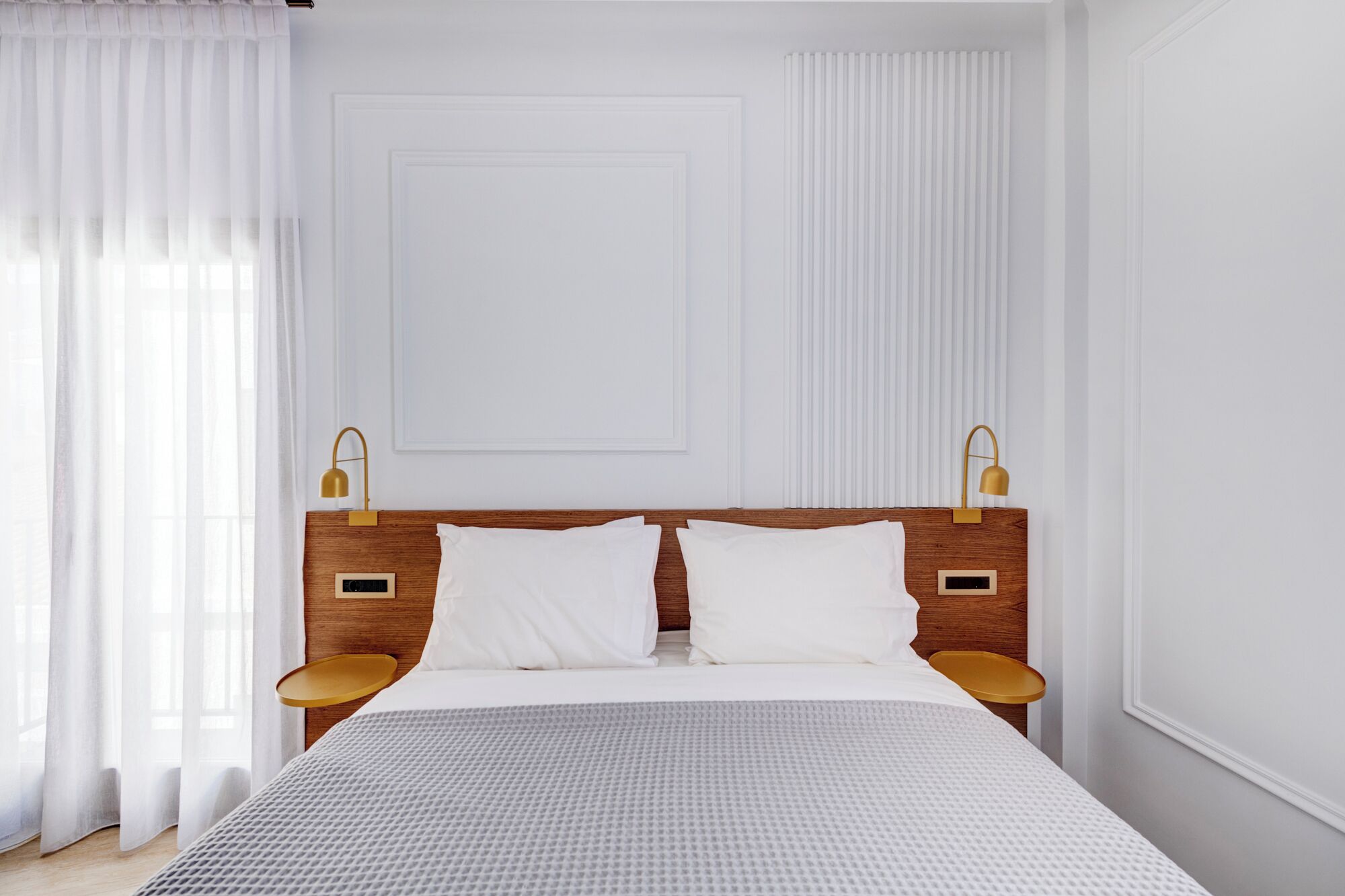 Quarto de hotel bem arrumado, com uma cama grande, duas mesas de cabeceira e uma cabeceira com painel de madeira.