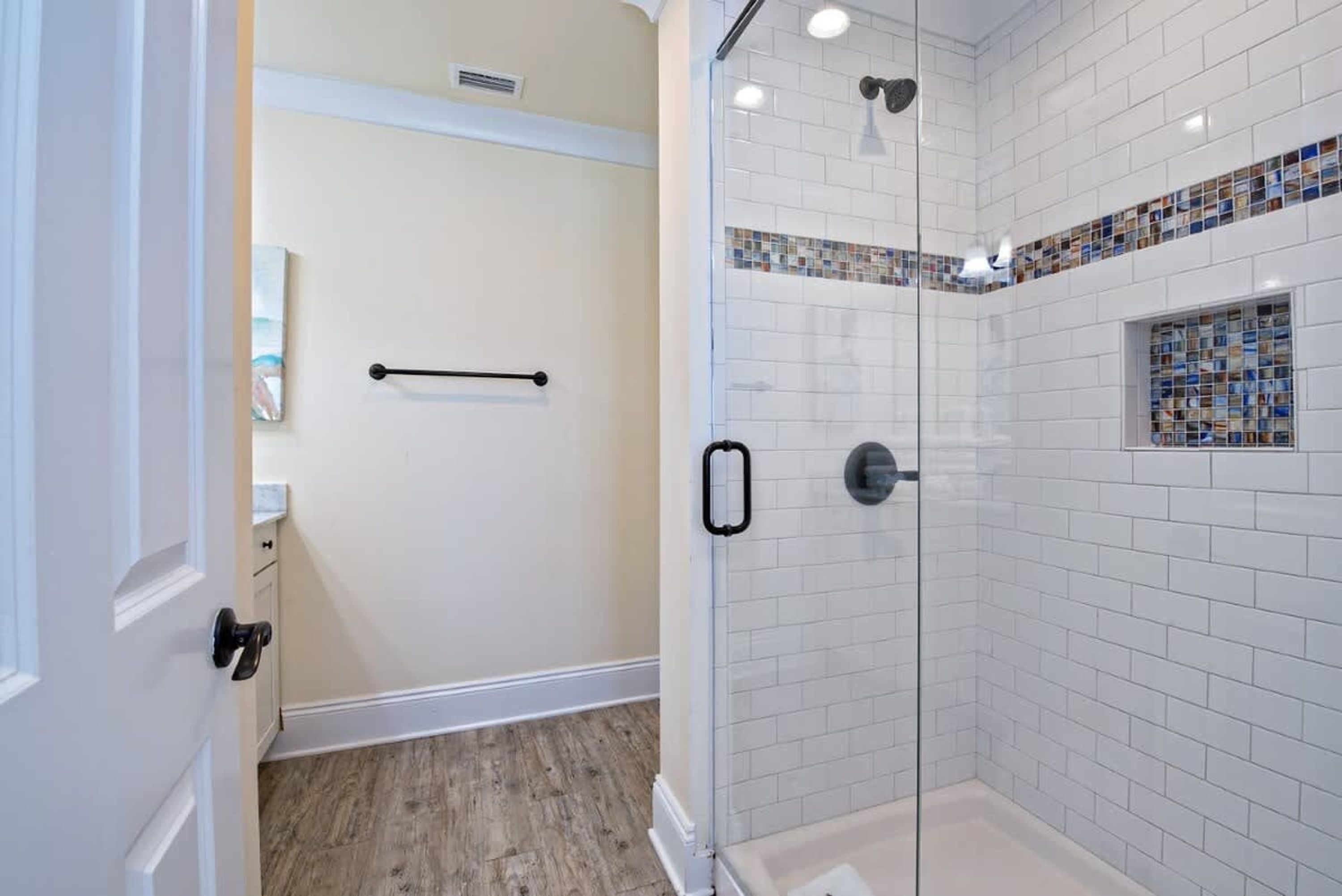 Um banheiro moderno com box de vidro, paredes com azulejos brancos e piso de madeira.