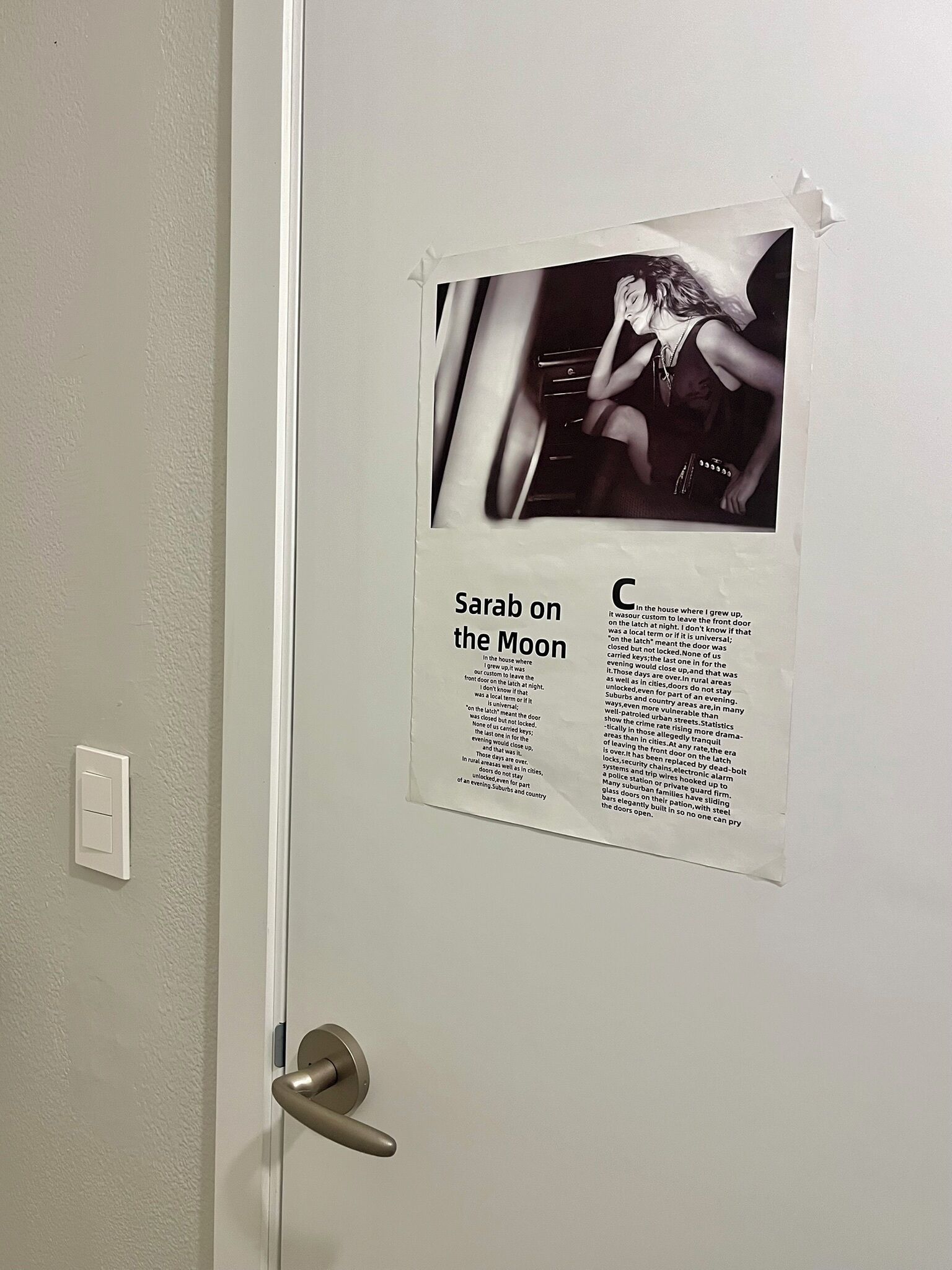 Uma porta com um cartaz de uma mulher sentada em uma cadeira, um puxador de porta e um interruptor de luz na parede.