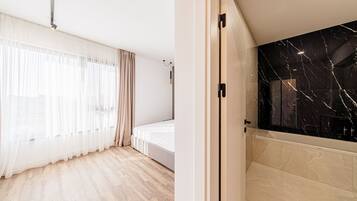 Quarto moderno com uma grande janela, uma cama e um banheiro com parede de mármore preto.