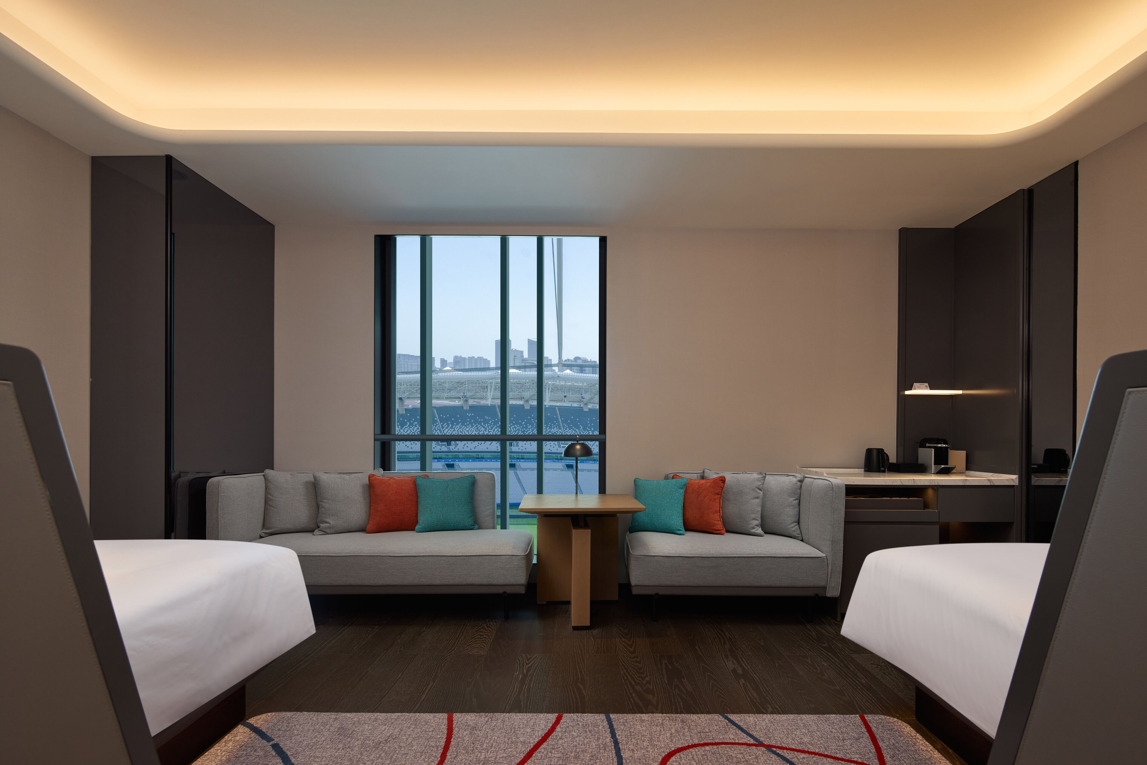 Quarto de hotel com duas camas, um sofá, uma mesinha e vista para a paisagem urbana.