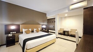 Quarto de hotel com uma cama grande, mesas de cabeceira, uma escrivaninha, duas cadeiras e um ar condicionado.
