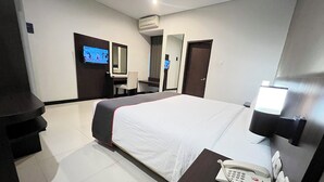 Quarto de hotel com cama, escrivaninha com telefone, televisão e espelho.