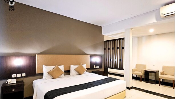 Quarto de hotel com cama grande, mesas de cabeceira, escrivaninha e área de estar com cadeiras e mesa.