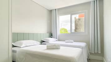 Quarto com duas camas de solteiro, janela com cortinas e vista para o exterior.
