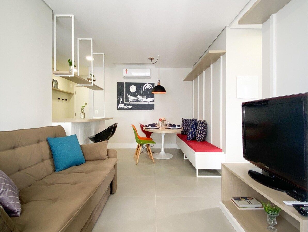 Uma sala de estar moderna com sofá, mesa de jantar com cadeiras, televisão de tela plana e prateleira fixada na parede.