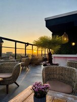 Um terraço no telhado com móveis de vime, um vaso de planta e um lustre.