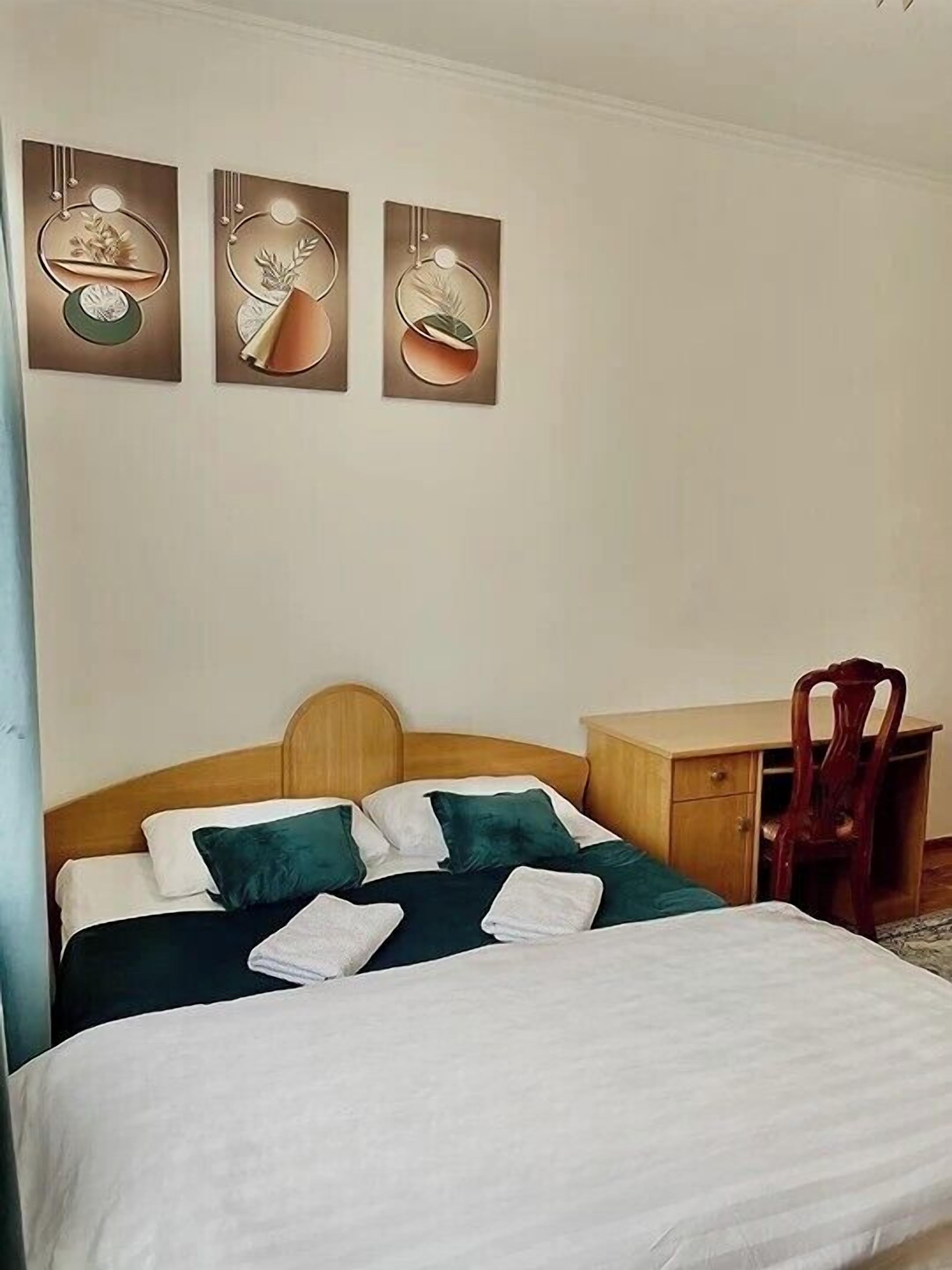 Quarto de hotel com cama, escrivaninha e cadeira. Três objetos decorativos fixados na parede acima da cama.