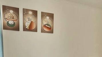 Quarto de hotel com cama, escrivaninha e cadeira. Três objetos decorativos fixados na parede acima da cama.