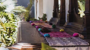 Um banco de madeira com almofadas coloridas e um tapete estampado, cercado por vegetação.