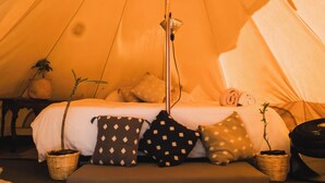 Interior acolhedor de uma tenda, com cama, almofadas, uma luminária pendente e um tapete tecido.