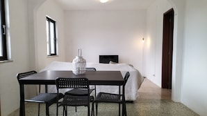 Um quarto com uma cama, uma mesa com cadeiras, um abajur e uma televisão.