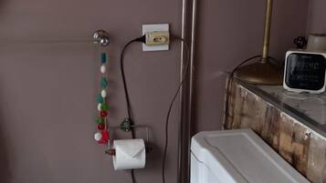 Um banheiro com vaso sanitário, pia fixa na parede, quadro emoldurado, luminária e relógio.
