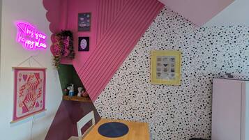Um quarto com parede salpicada em rosa e branco, um letreiro de neon e um quadro com um jogo de cartas.