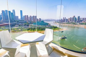Quarto de hotel moderno com uma grande janela que oferece vista para o horizonte urbano, um rio e uma ponte.