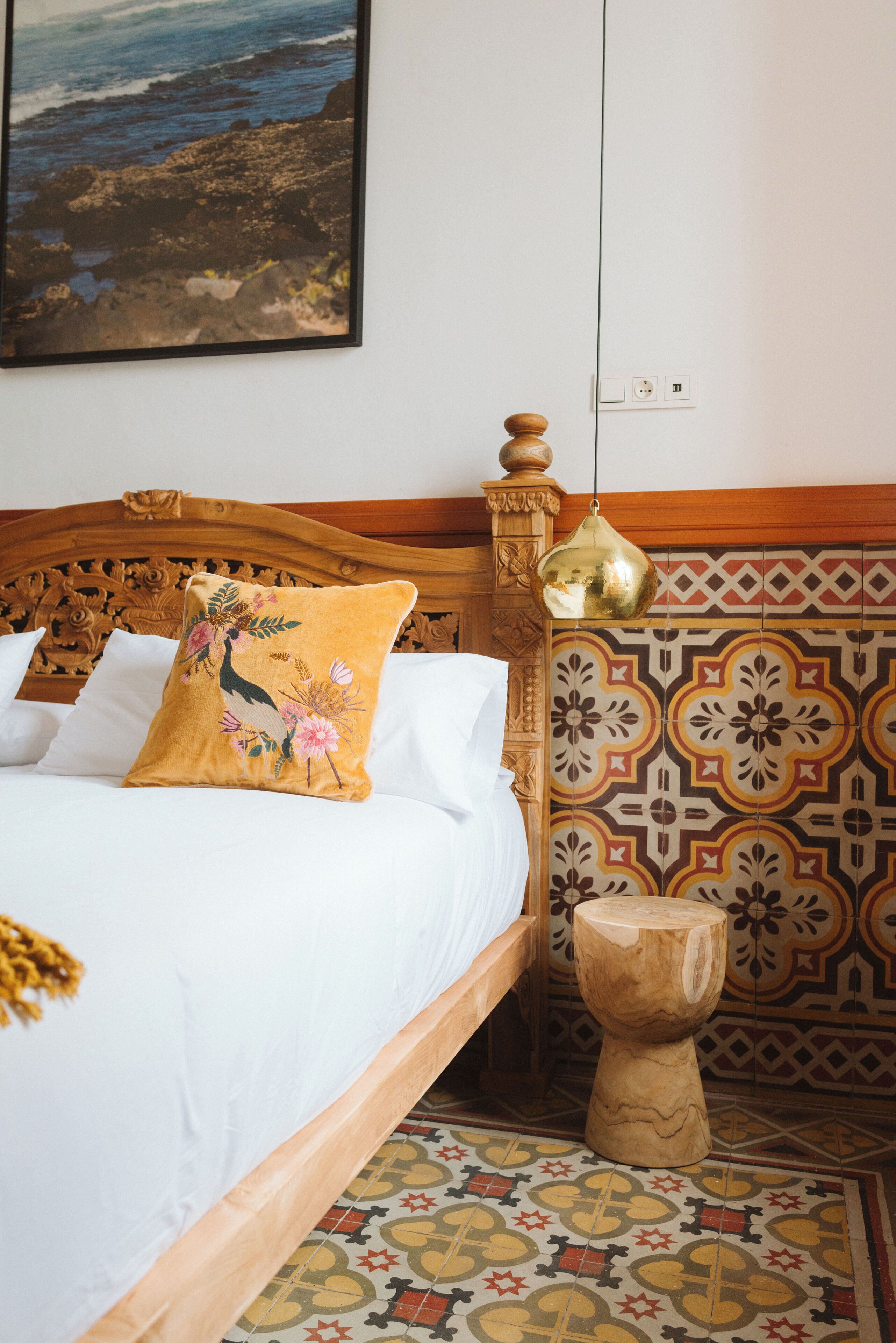 Cama com cabeceira de madeira, almofada decorativa, luminária pendente e parede estampada.