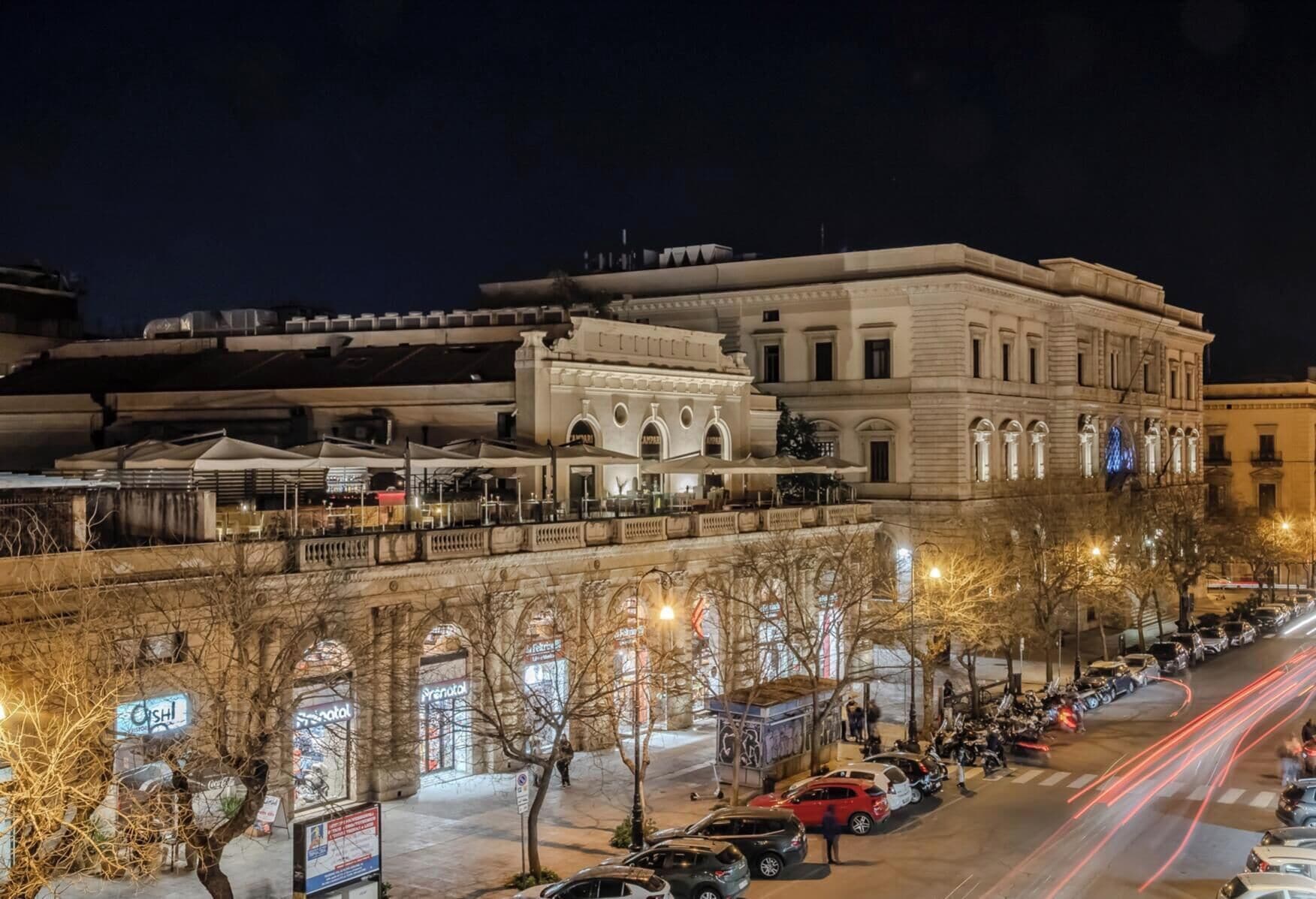 Vista noturna de um edifício com estilo arquitetônico clássico, com janelas em arco e varanda.