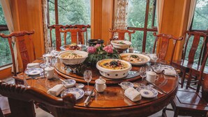 Uma mesa de jantar redonda posta com diversos pratos, rodeada por cadeiras de madeira com entalhes elaborados.