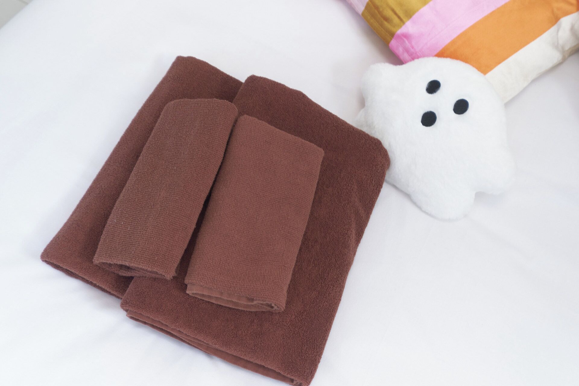 Uma cama com toalhas castanhas dobradas e um brinquedo macio branco.