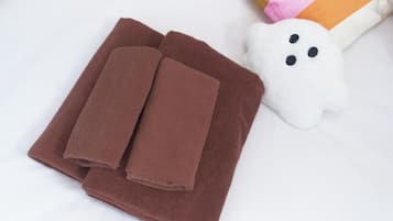 Uma cama com toalhas castanhas dobradas e um brinquedo macio branco.