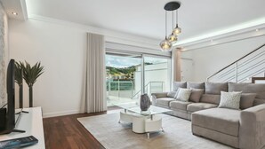 Uma sala de estar moderna com um sofá, uma mesa de centro de vidro e uma televisão em um suporte.