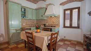 Uma cozinha com piso ladrilhado, armários de madeira, uma mesa com cadeiras e uma janela com persianas.