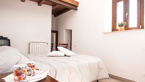 Quarto com cama, mesa de cabeceira e janela com uma planta.
