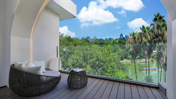 Varanda com vista para um lago, cercada por vegetação e montanhas.
