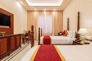 Quarto de hotel com duas camas, televisão, escrivaninha e janela com cortinas.