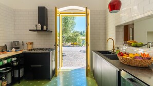 Cozinha moderna com vista para um jardim, uma luminária pendente vermelha e uma cesta de frutas na bancada.