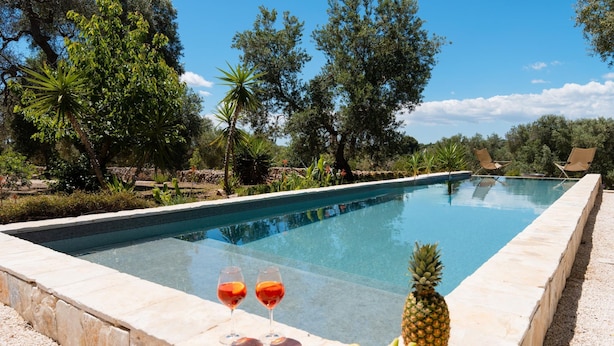 Piscina com borda de pedra, duas espreguiçadeiras e uma bandeja com frutas e bebidas na beira da piscina.